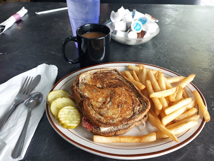 The Reuben&mdash;architectural marvel of sandwich engineering. Golden-grilled rye supporting a skyscraper of corned beef with pickle reinforcements standing guard.