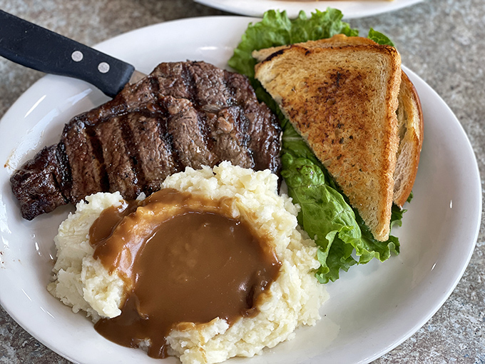 A steak that doesn't need fancy presentation to impress, just perfect grill marks and mashed potatoes swimming in gravy that whispers, "Nap time soon."