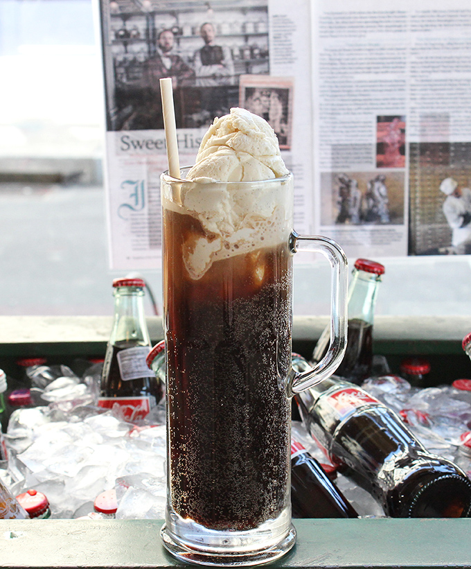 The root beer float: where carbonation meets creaminess in a tall glass tango. Those vintage bottles in the background aren't just decoration&mdash;they're co-conspirators.