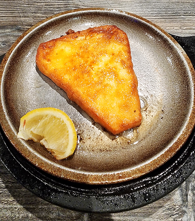 Golden saganaki arrives sizzling like a delicious firework show, proving cheese can indeed be pure theater on a plate.