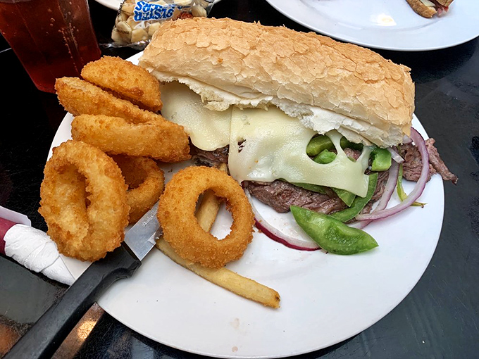 This isn't just a sandwich—it's a structural marvel of melted cheese, crisp vegetables, and perfectly seasoned beef, flanked by golden onion rings that shatter satisfyingly with each bite.