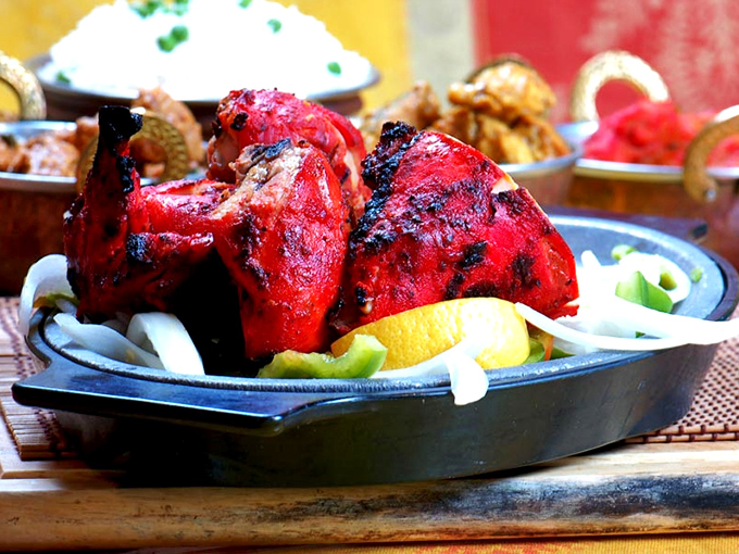 Tandoori chicken so vibrantly red it could stop traffic, with char marks that tell stories of ancient cooking techniques and patient marination.