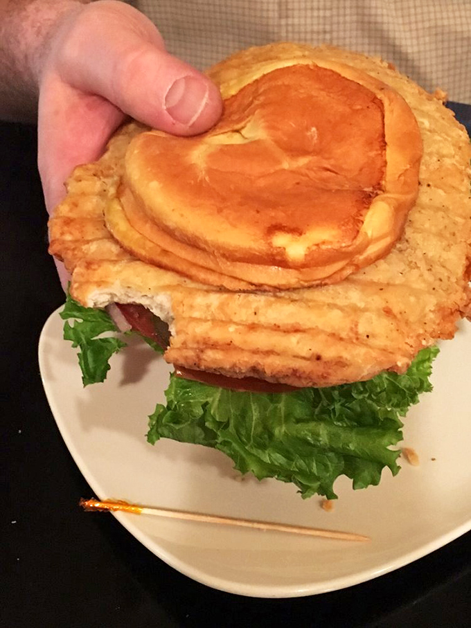 Indiana's famous pork tenderloin sandwich in its natural habitat—comically oversized and refusing to acknowledge the boundaries of its plate.