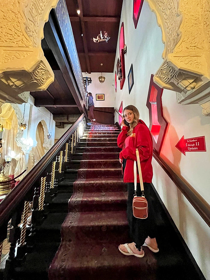 The grand staircase invites exploration upward, its rich burgundy carpet and carved wooden railings guiding visitors toward the second floor's treasures.