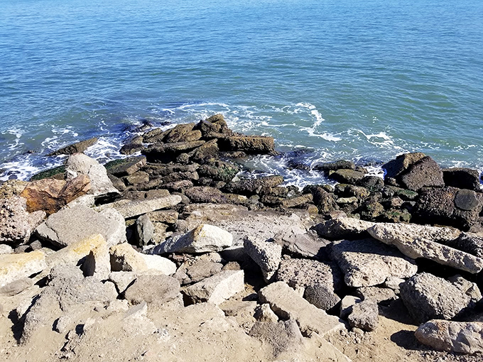 Nature's demolition crew meets human creativity where waves crash against this rocky shoreline, creating the percussion section.