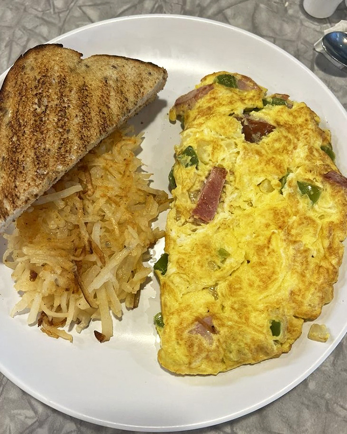 Behold the Western omelet in its natural habitat—perfectly folded, generously stuffed, and flanked by hash browns that achieved the crispy-tender paradox.