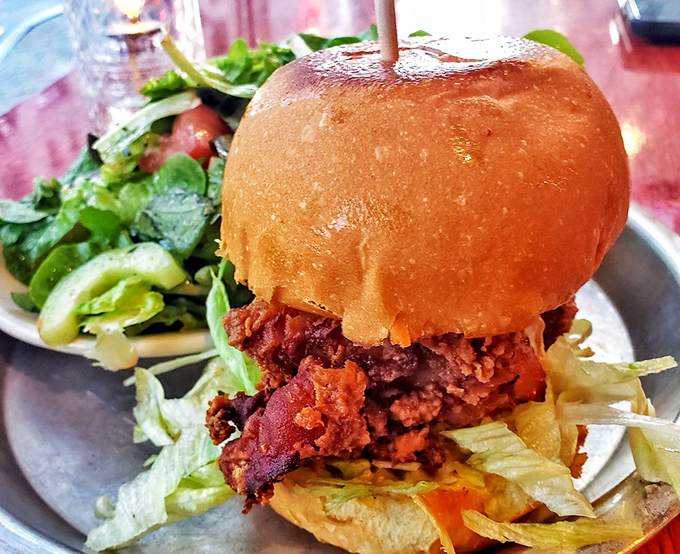 The holy grail of chicken sandwiches arrives on a gleaming metal plate, its golden bun crowning crispy perfection like a delicious halo.