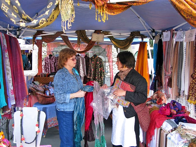 A colorful textile booth where scarves and fabrics from around the world transform the parking lot into an international bazaar of color and texture.