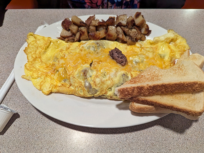 Behold the omelet in its natural habitat – perfectly folded, cheese melting seductively, home fries crisped to golden perfection. Breakfast nirvana achieved.