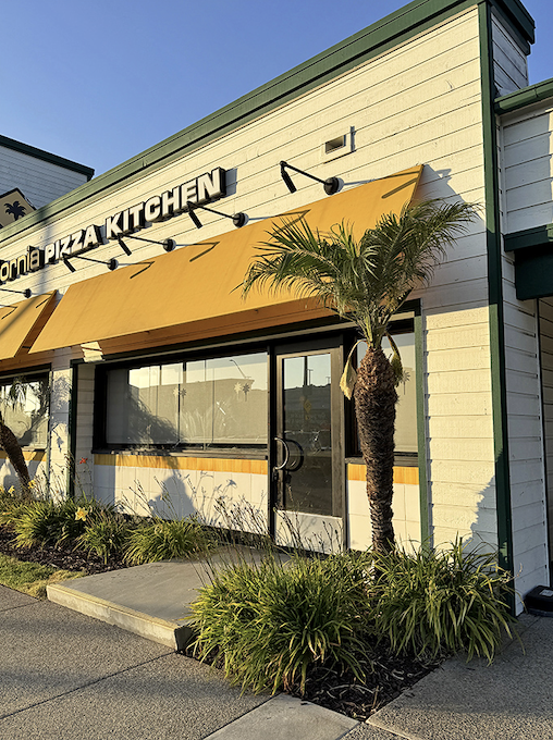 Sunlight plays across CPK's welcoming entrance, where the promise of creative California-inspired pies awaits beach-goers and locals alike.