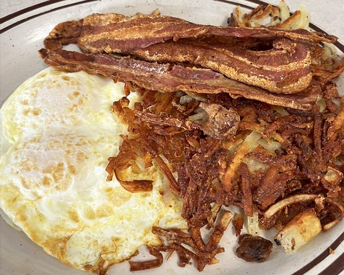 Simplicity perfected: two sunny-side up eggs beside hash browns so crispy they practically audition for a potato chip commercial. That bacon deserves its own fan club.