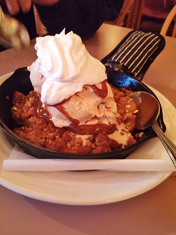 Dessert that demands attention: a skillet apple crisp crowned with vanilla ice cream, whipped cream, and caramel drizzle—like autumn decided to throw itself a party.