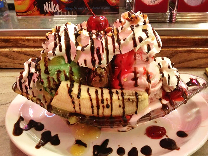 The banana split arrives like royalty on a boat-shaped throne, dressed to the nines in whipped cream finery.