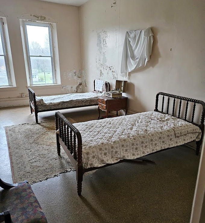 Two narrow beds with vintage frames tell stories of shared quarters and lost privacy. The peeling walls have absorbed decades of whispered confessions.