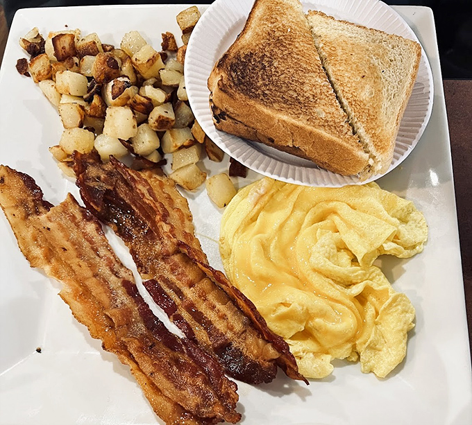 The breakfast trinity: perfectly scrambled eggs, toast with that ideal butter-to-bread ratio, and bacon that's achieved crispy nirvana. Home fries playing the essential supporting role.