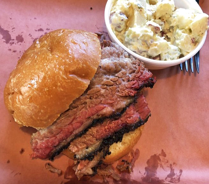 A brisket sandwich that requires both hands and possibly a liability waiver. The smoke ring is so perfect it could be framed in an art gallery.