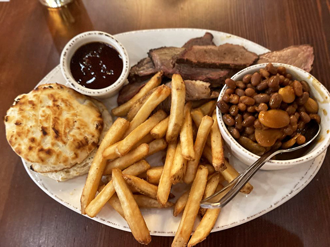 The holy trinity of BBQ sides&mdash;golden fries, savory beans, and a buttery biscuit&mdash;flanking slices of brisket with that telltale pink smoke ring of perfection.