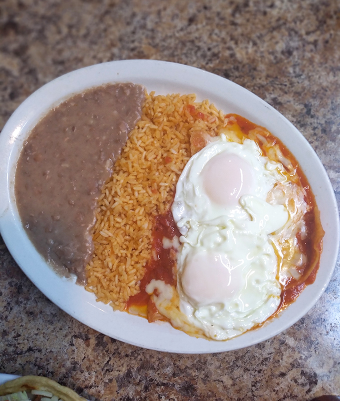 Huevos rancheros done right – sunny-side eggs nestled in vibrant salsa, with rice and beans standing by for the perfect bite.