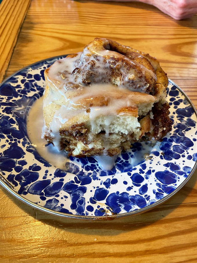This cinnamon roll isn't just dessert pretending to be breakfast&mdash;it's a gooey, glazed monument to morning indulgence on a blue-speckled plate.