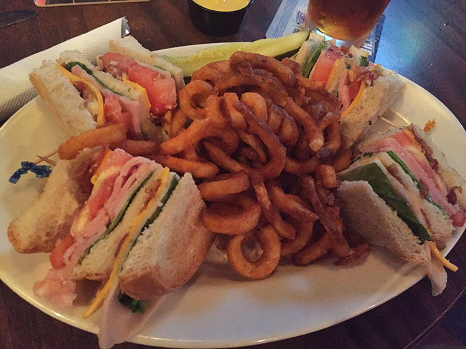 The club sandwich arrives like a skyscraper of flavor, surrounded by a moat of curly fries that disappear faster than you'd admit.