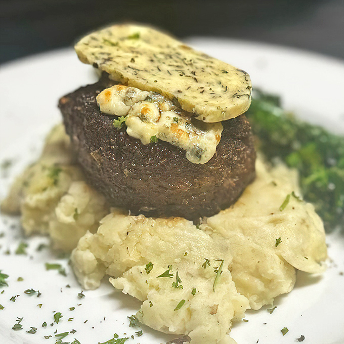 Filet mignon perched atop mashed potatoes like royalty on a cloud. That herb butter melting down the sides is nature's perfect sauce.