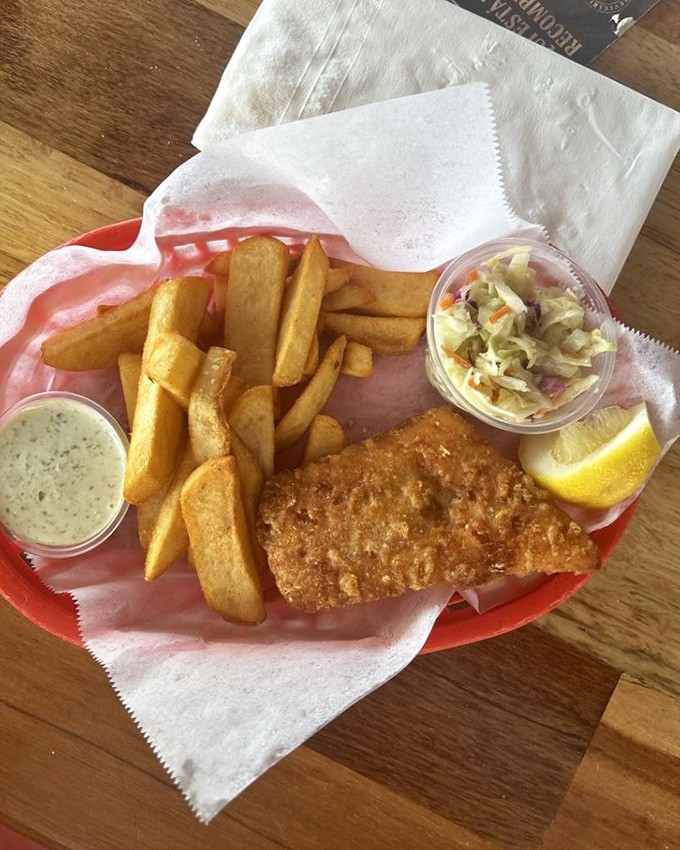 Golden-battered fish resting on a bed of crispy fries with coleslaw standing by. The paper liner isn't pretentious&mdash;it's a promise of proper seafood.