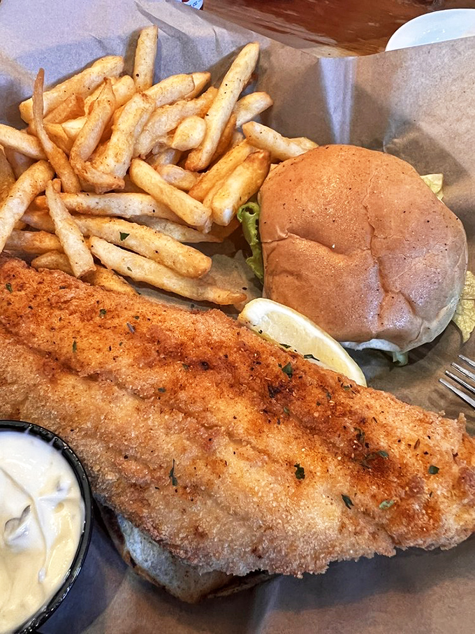 Golden-fried flounder that breaks apart with the gentlest pressure, nestled in a bun with fries that demand to be savored, not rushed.