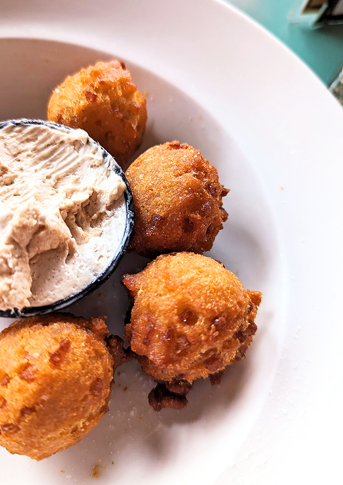 Golden hush puppies with a side of what appears to be seafood spread – Southern comfort in spherical form.