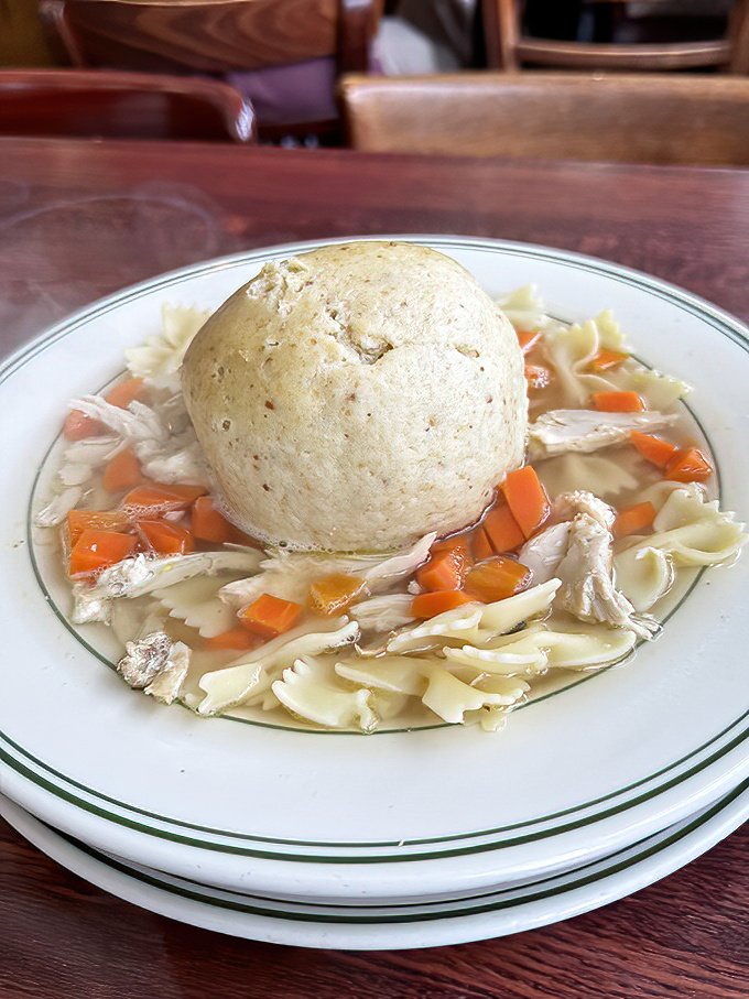 One matzo ball, big enough to have its own zip code, swimming in golden broth like edible comfort.