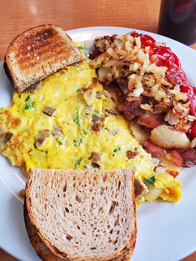 Breakfast architecture at its finest: a fluffy omelet foundation, crispy home fries support beams, and toast buttresses. Engineering you can eat.