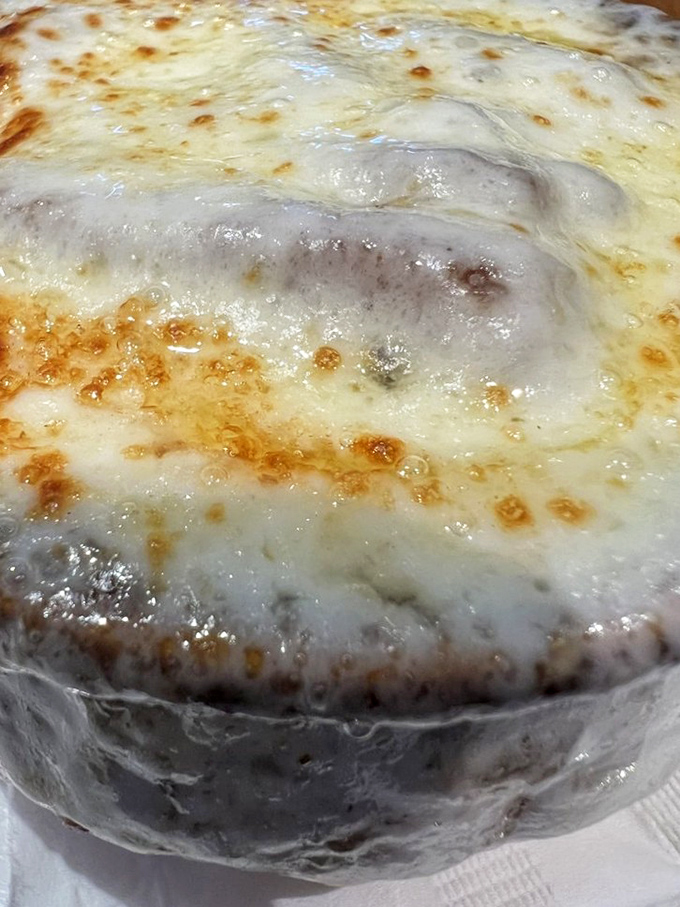 Beneath that bubbling cheese canopy lies a savory French onion soup so rich it should come with its own tax bracket.