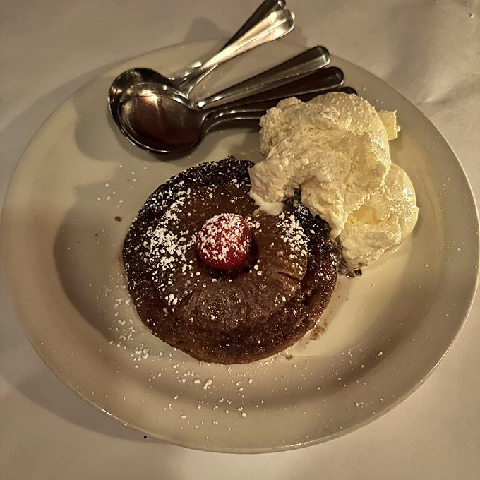 Dessert that demands respect: warm chocolate cake crowned with a raspberry, dusted with powdered sugar, and escorted by whipped cream.