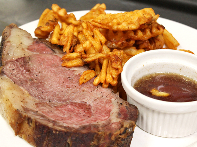 The prime rib arrives like a pink-centered revelation, perfectly seasoned and accompanied by golden waffle fries and that essential au jus.