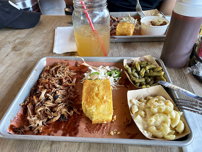 A metal tray loaded with smoky treasures&mdash;pulled pork, cornbread, green beans, and mac and cheese. Silverware optional, napkins mandatory.