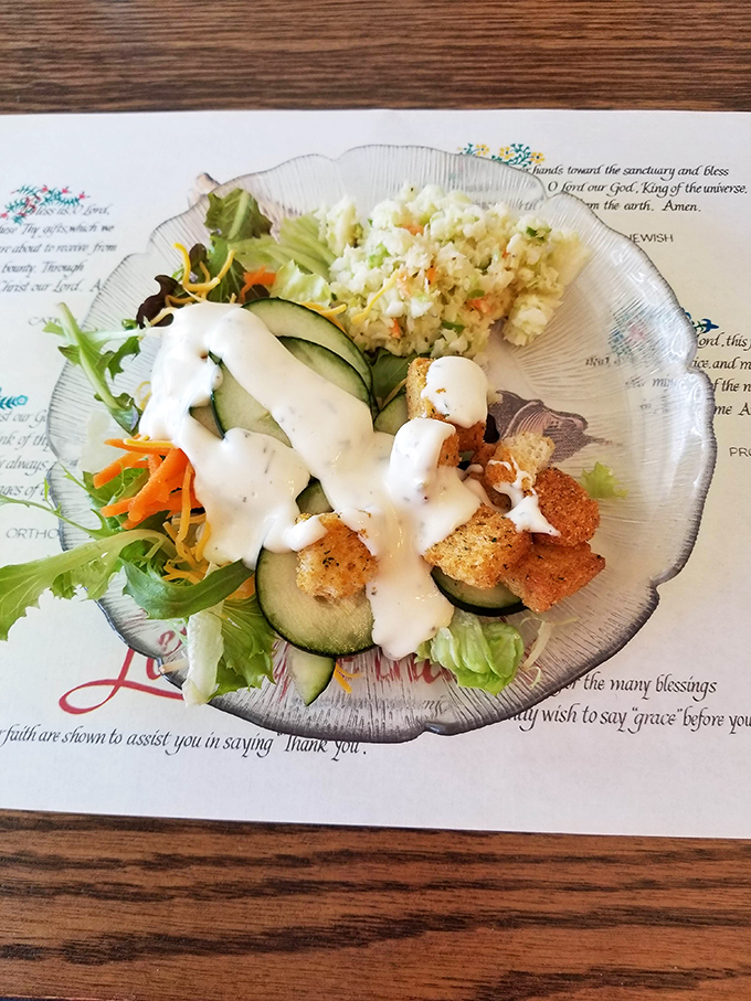 A salad that actually deserves attention! Fresh greens, crisp vegetables, and house-made potato salad on a prayer-adorned placemat&mdash;nourishment for body and soul.