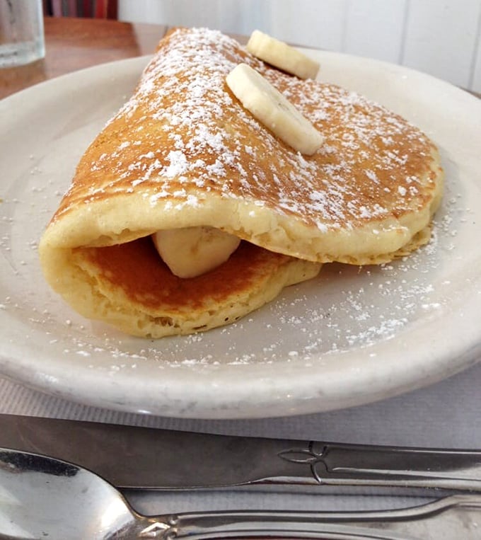 Pancakes folded like love letters around fresh bananas, dusted with powdered sugar snow. Breakfast poetry on a plate.