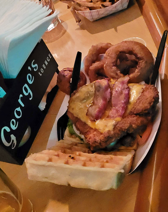 Crispy chicken perched on a golden waffle with onion rings standing guard &ndash; breakfast and dinner having a delicious identity crisis.