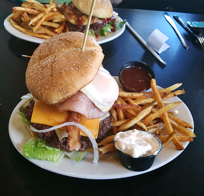 Behold the burger in its natural habitat&mdash;accompanied by golden fries and house-made dipping sauces. The toothpick isn't decoration; it's structural engineering for this towering masterpiece.