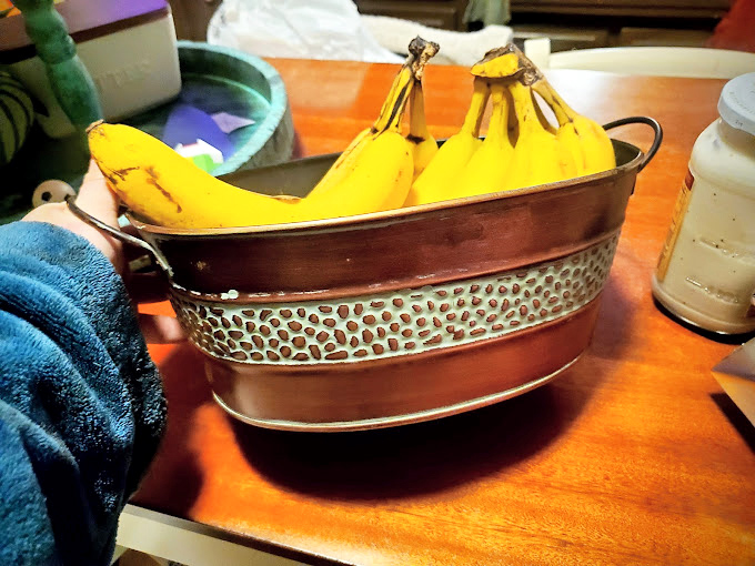 A vintage copper basin cradles bananas with unexpected elegance. Someone's kitchen castoff becomes another's Pinterest-worthy find.