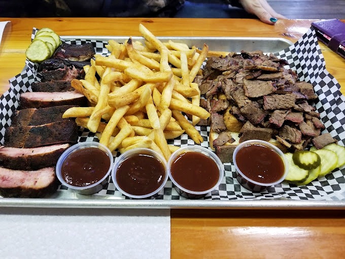 A barbecue platter that doubles as an edible work of art&mdash;sliced brisket and pulled pork flanking golden fries, with sauce cups standing guard.