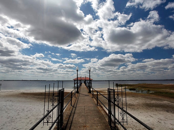 A long pier stretches over calm waters under dramatic clouds, offering a peaceful spot for fishing or contemplation.