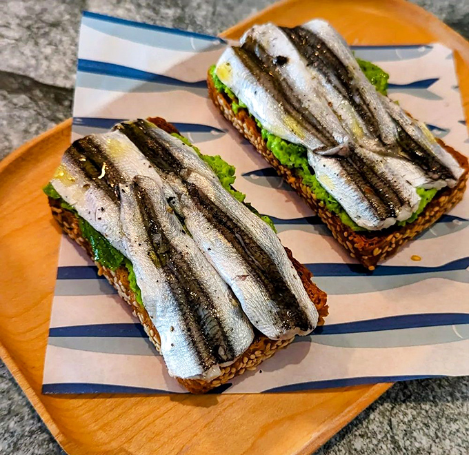 Anchovies lounging on seeded toast like tiny silver celebrities on a red carpet. This is what bread dreams of becoming when it grows up.