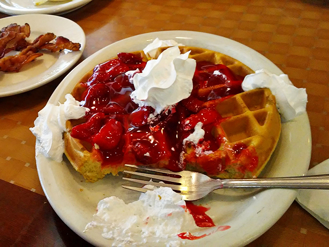 A Belgian waffle that's having more fun than you are, topped with strawberries and whipped cream islands slowly melting into berry-filled valleys.