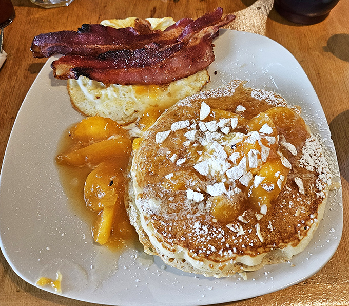 Pancakes with that ideal golden-brown exterior, topped with powdered sugar and served with caramelized peaches that taste like summer memories. Plus bacon, because obviously.
