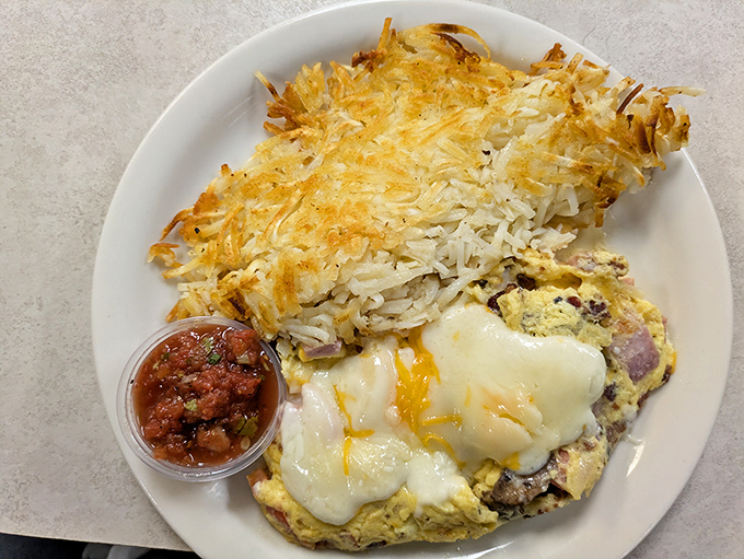 A hearty breakfast plate featuring a fluffy omelet smothered in cheese alongside crispy hash browns and salsa&mdash;morning fuel that means business.