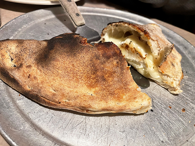 The calzone, caught mid-bite, reveals its molten cheese interior&mdash;like nature documentaries showing lava flowing from volcanoes, but much more delicious. 