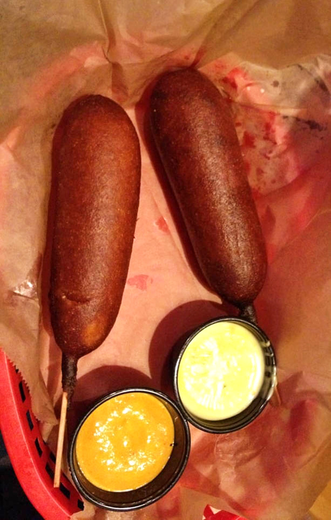 Two perfectly bronzed corn dogs stand at attention, flanked by dipping sauces like royal guards protecting delicious treasure.