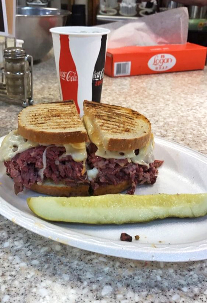 The Reuben in its natural habitat: a simple white plate where corned beef, sauerkraut, and Swiss cheese achieve perfect harmony.