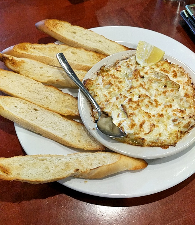 The crab dip arrives with a golden-brown crust that gives way to creamy decadence beneath. Those toasted baguette slices? The perfect delivery system.