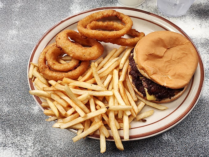 The classic American trinity: golden fries, onion rings, and a cheeseburger on a plate with the brown stripe that's in every grandma's china cabinet.